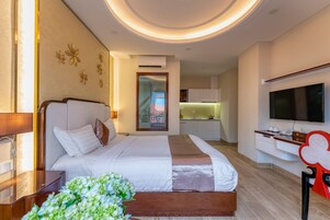 Quarto de hotel com cama, mesa de cabeceira, televisão e vista para a cozinha e varanda.