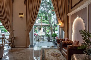 Um hall de hotel com área de estar, uma janela grande com cortinas, e vista para a rua.