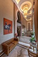 Um hall luxuoso com um sofá de couro marrom, um candelabro e um espelho grande que reflete o espaço.