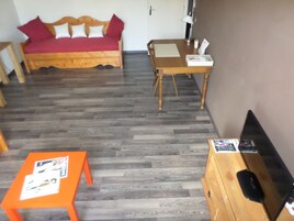 Quarto com sofá de madeira, mesa de jantar, mesa laranja e armário de madeira com um rato de computador.