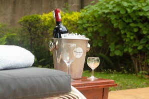 Um balde de metal com uma garrafa de vinho e um copo sobre uma mesa de madeira ao ar livre.