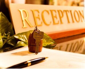 Um balcão de recepção com uma placa indicando "RECEPTION", chaveiro e caneta sobre uma superfície com folhas verdes.