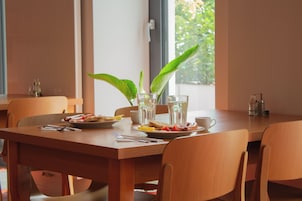 Uma mesa de jantar com cadeiras, pratos de comida, copos e um vaso de planta.