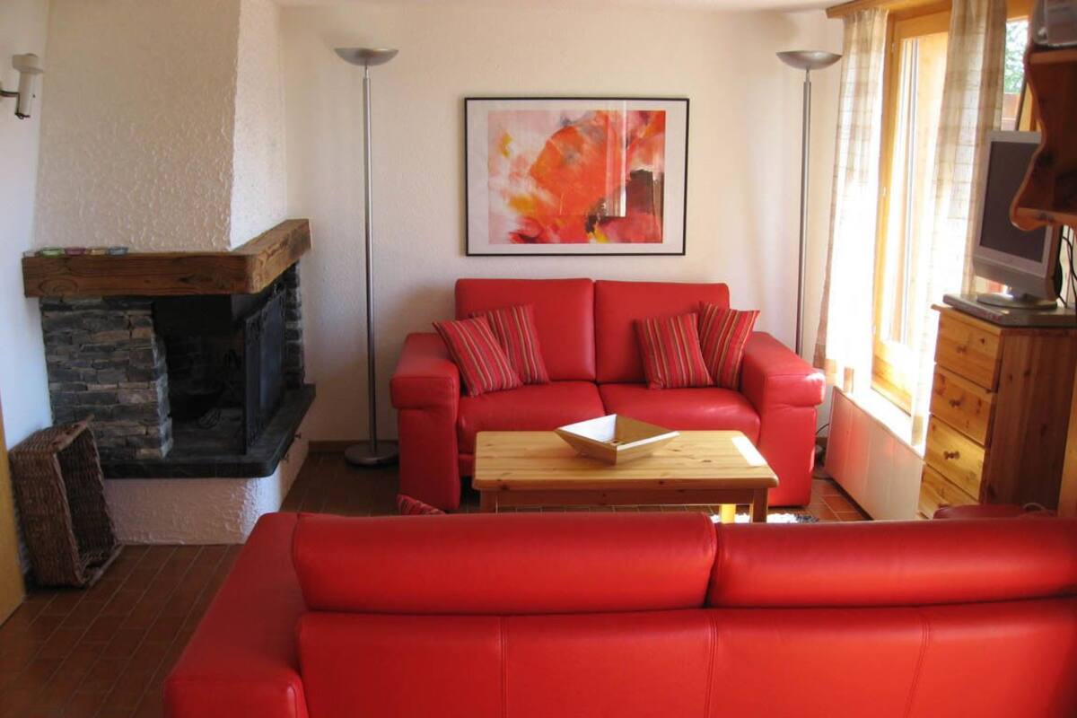 Uma sala de estar com um sofá vermelho, uma mesa de centro de madeira, uma lareira e um quadro na parede.