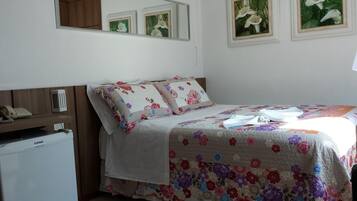 Quarto com cama, mesa de cabeceira com telefone e pequeno frigorífico.