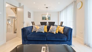 Uma sala de estar moderna com um sofá azul, uma mesa de centro e um espaço de jantar com cadeiras.