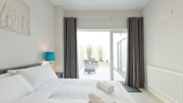 Quarto de hotel com cama, dois toalhas enrolados, uma luminária e vista para um pátio externo.