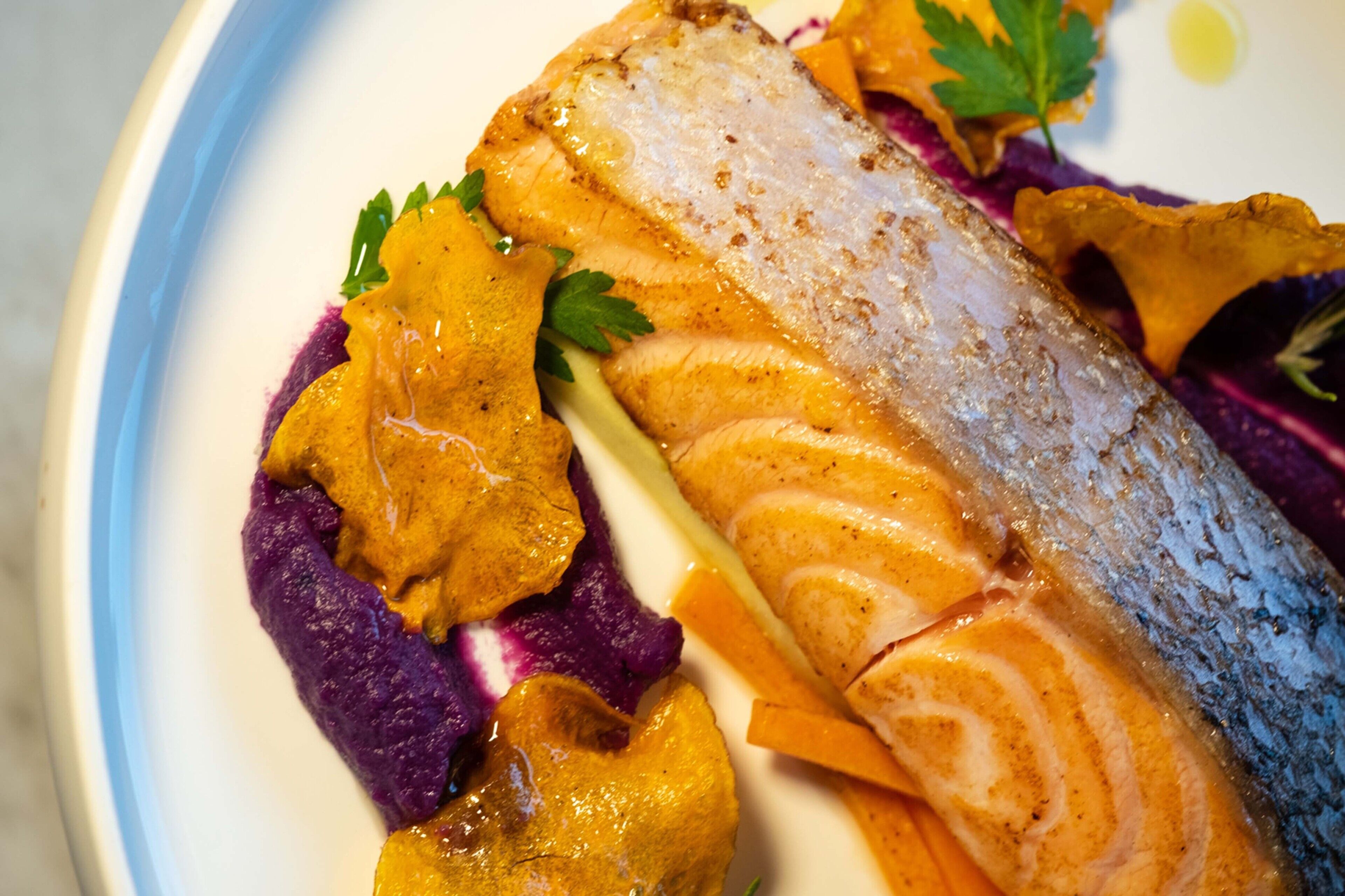 Um prato com filé de peixe, legumes roxos e laranjas e um enfeite.