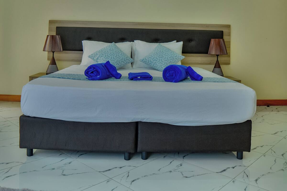 Uma cama bem arrumada com cabeceira, duas luminárias de apoio e um quadro na parede.