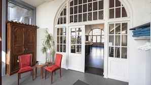 Um saguão com uma ampla janela em arco, um armário de madeira, duas cadeiras vermelhas e uma mesa pequena.