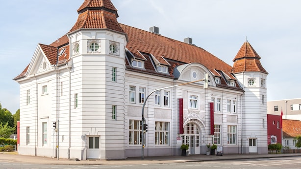 Um edifício grande e histórico, com fachada simétrica, várias janelas e uma entrada central com arco decorativo.