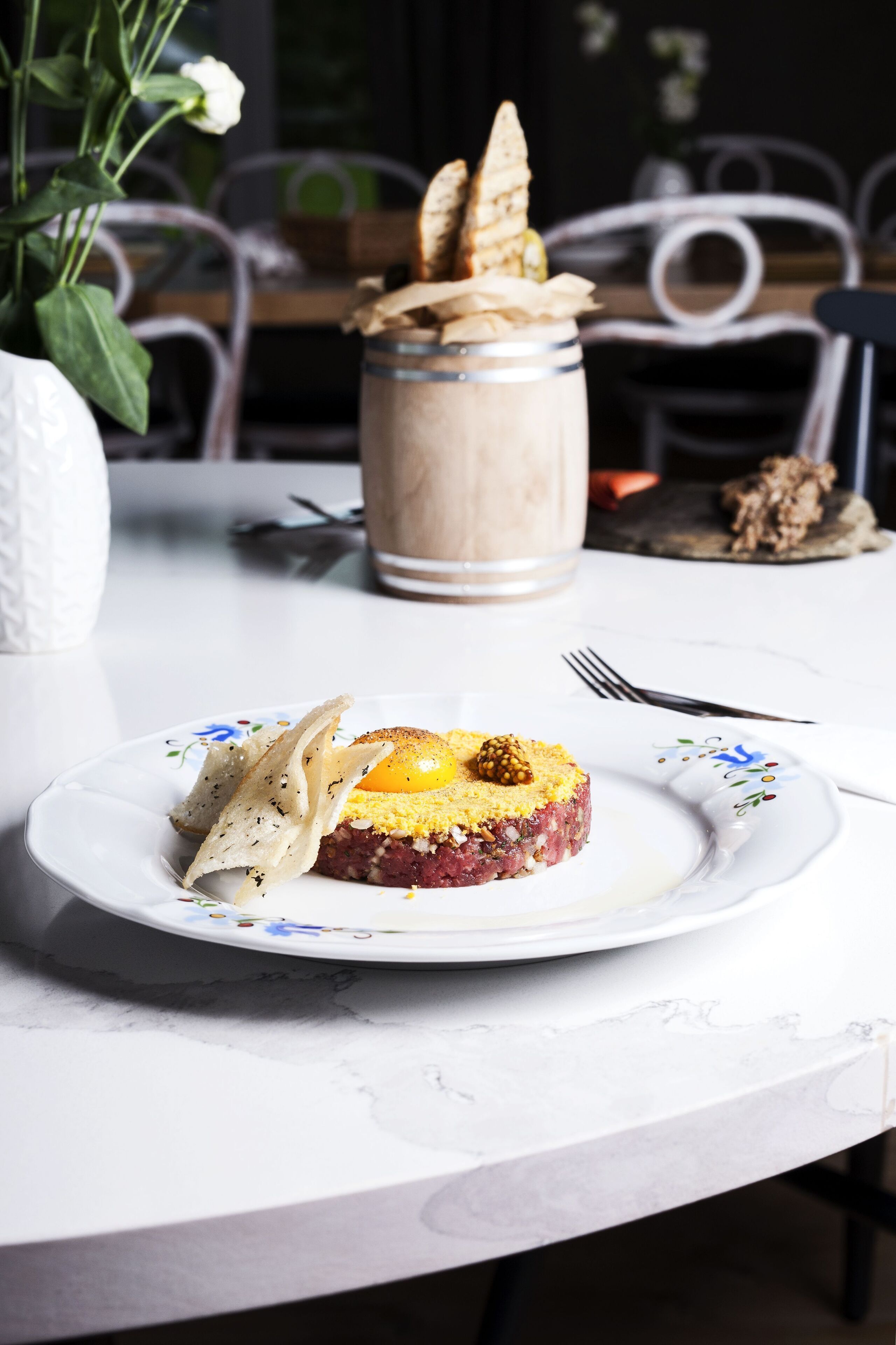Um prato com comida, um pote e um garfo sobre uma mesa.