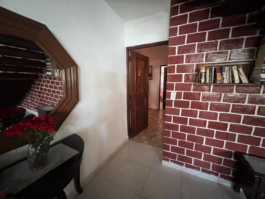 Um corredor com parede de tijolos, escada de madeira e porta que dá para outro cômodo.