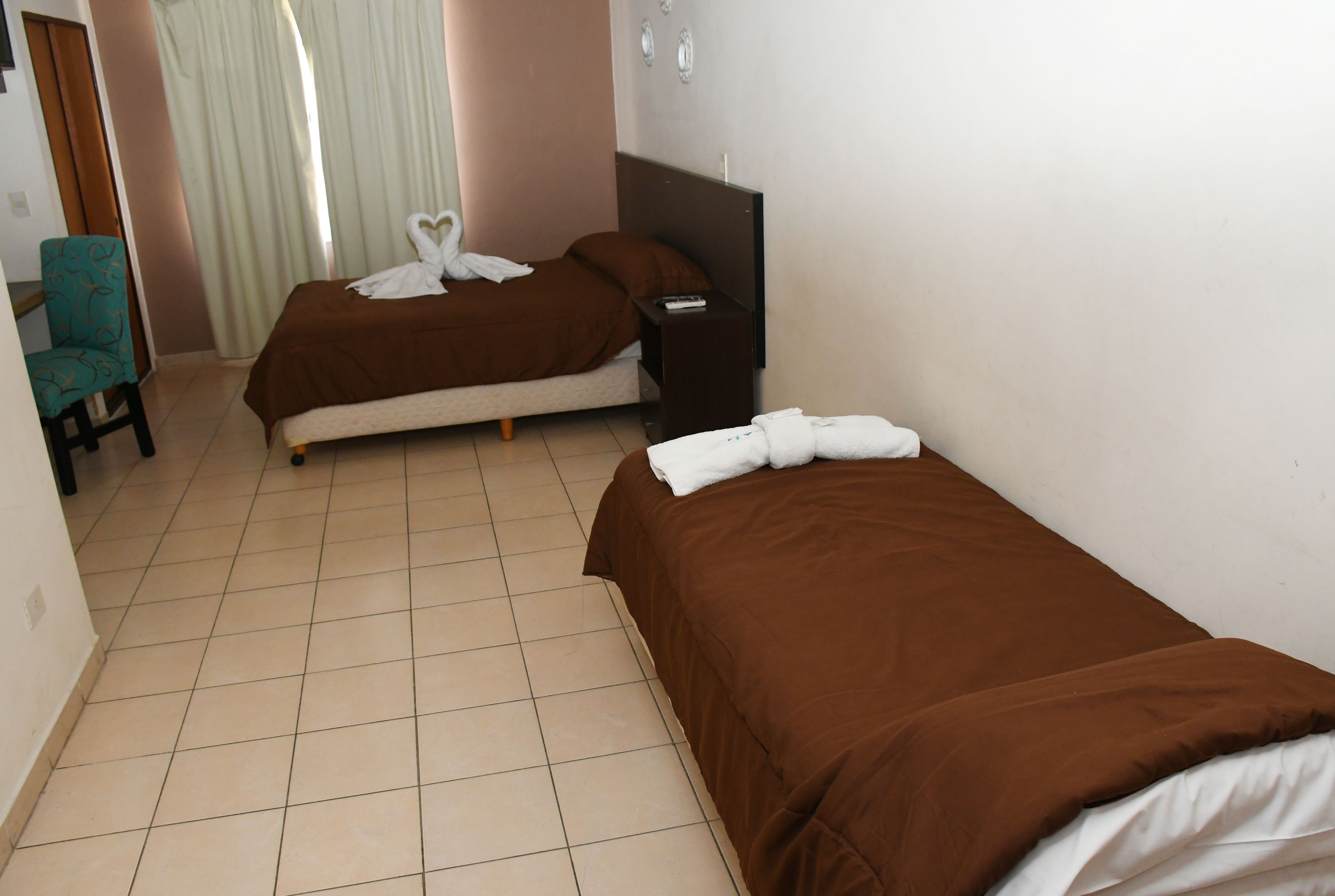Quarto de hotel com duas camas, uma cadeira e uma mesa de cabeceira.