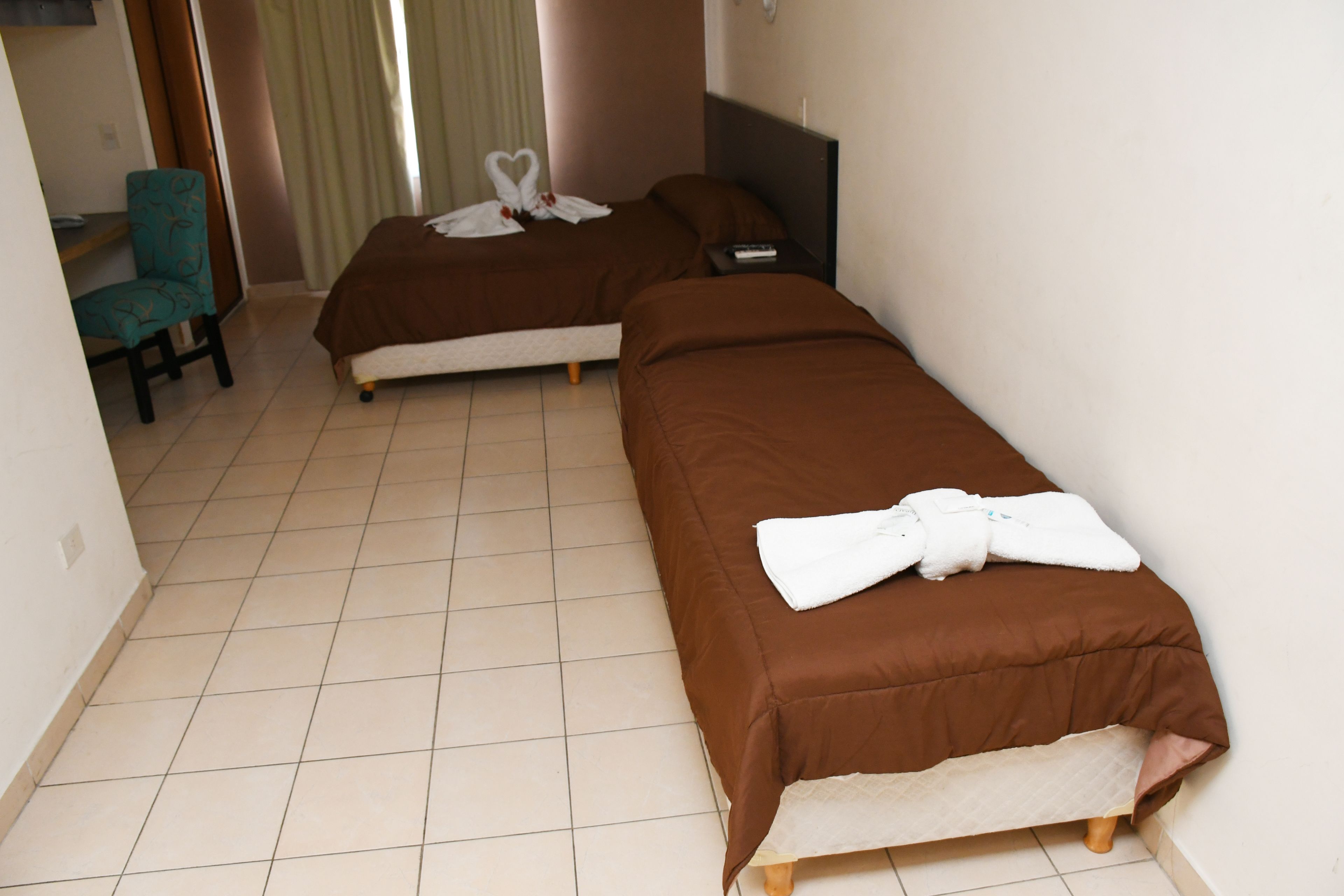 Quarto de hotel com duas camas, uma cadeira e uma televisão.