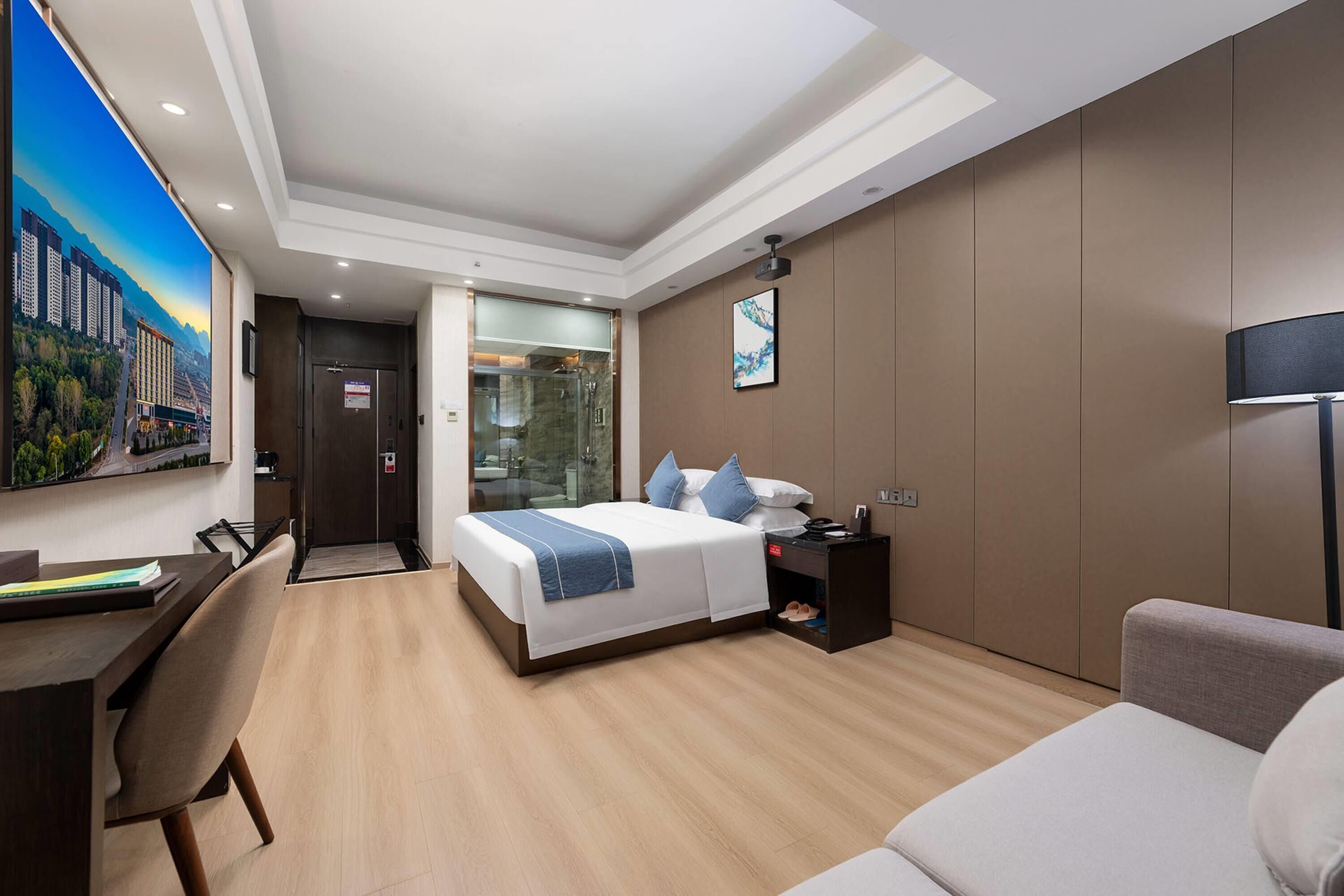 Quarto de hotel moderno com cama, escrivaninha, cadeira e televisão.