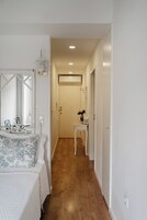 Um quarto com uma cama, mesa de cabeceira, espelho e porta que dá para um corredor.
