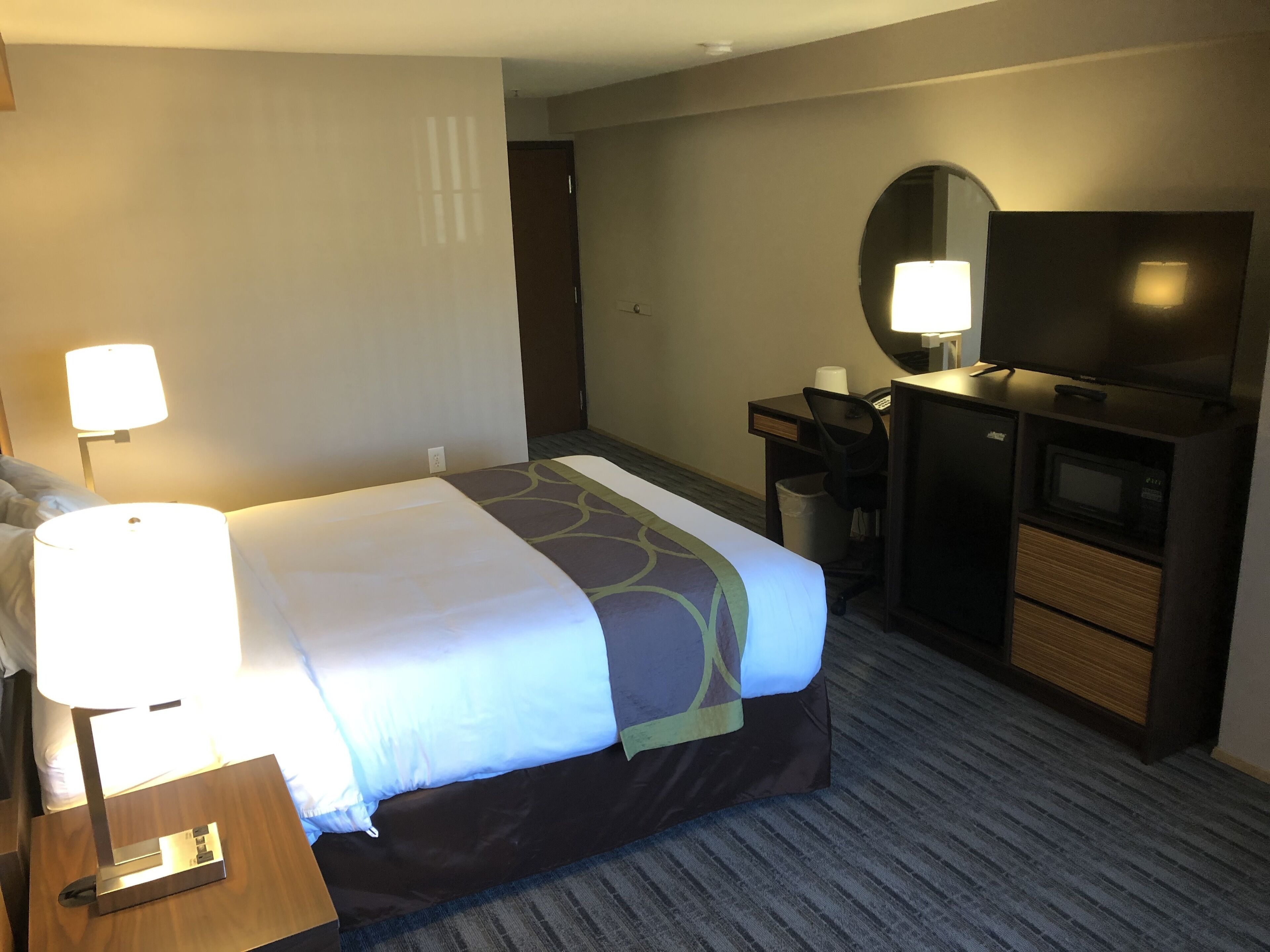 Quarto de hotel com cama, abajures, escrivaninha com cadeira, televisão e micro-ondas.