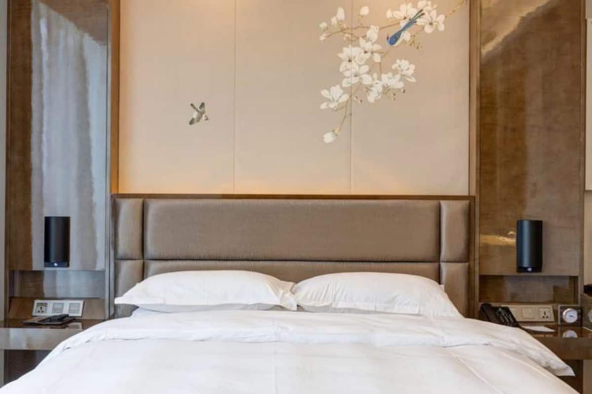 Quarto de hotel moderno com uma cama grande, paleta de cores neutras e um painel decorativo com motivos florais.