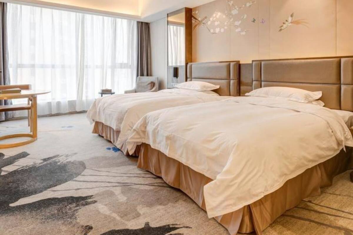 Quarto de hotel com duas camas, um espaço de estar e uma janela grande com cortinas.