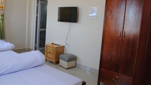 Quarto de hotel com uma cama, um guarda-roupa de madeira, uma televisão na parede e um pequeno móvel de madeira.