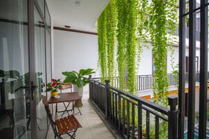 Varanda com porta de vidro, mesa de madeira, duas cadeiras e plantas em vasos.