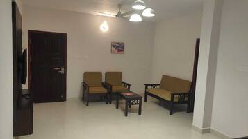 Sala de estar com sofá, duas poltronas, mesa de centro, ventoinha no teto e uma porta.