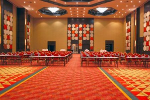 Uma sala de conferências com fileiras de mesas e cadeiras, um carpete estampado e uma parede decorativa com desenhos circulares.