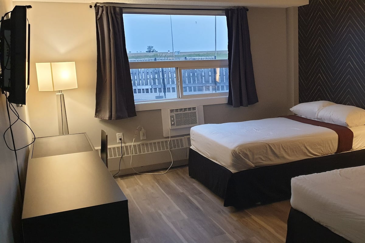 Quarto de hotel com duas camas, uma janela grande com cortinas, aquecedor fixado na parede e uma televisão sobre um suporte.