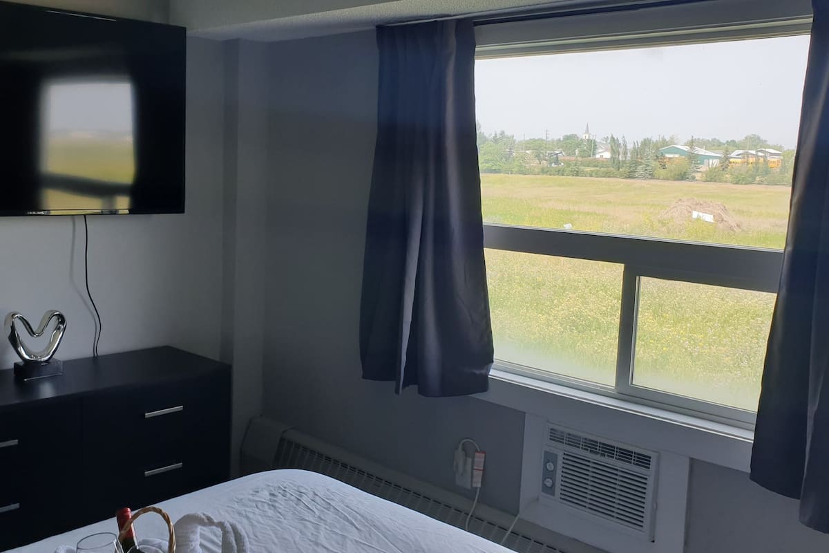 Quarto de hotel com uma cama, uma TV fixada na parede, um móvel escuro e uma janela com cortinas.