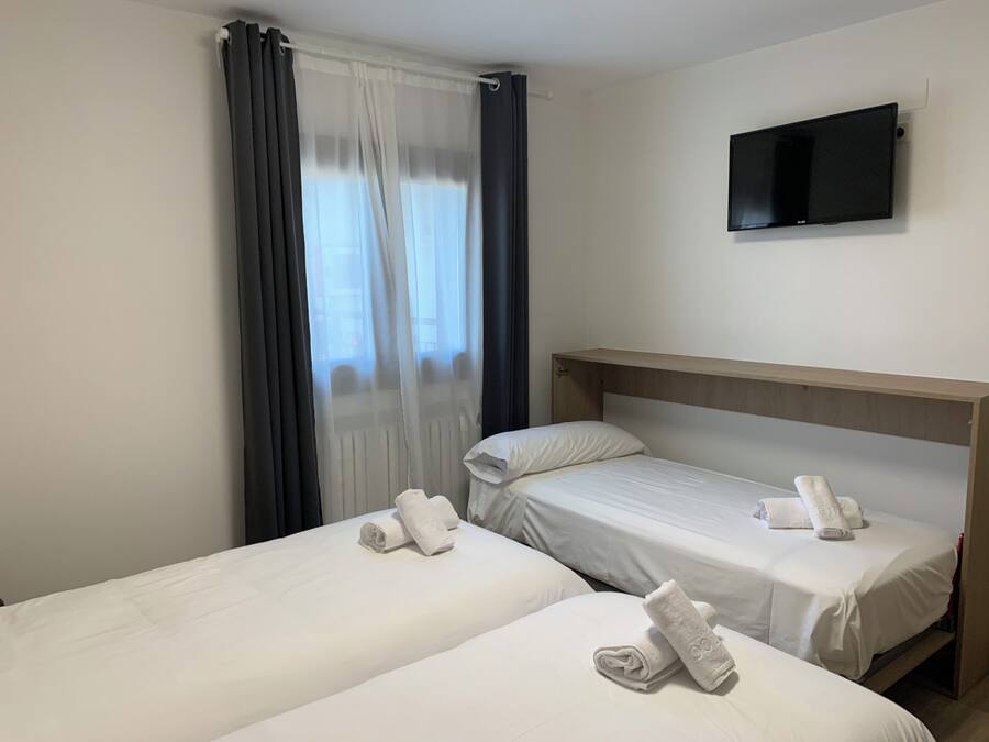 Quarto de hotel com duas camas de solteiro, televisão fixada na parede e janela com cortinas.