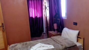 Quarto de hotel com duas camas, janela com cortinas, mesa de cabeceira e ar condicionado.