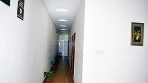 Um corredor com piso de madeira, plantas em vasos, sinal de vigilância e quadros nas paredes.