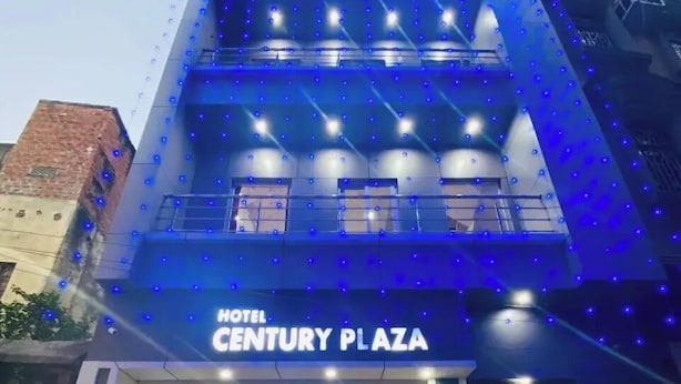 Entrada de hotel com uma placa indicando 'HOTEL CENTURY PLAZA', luzes decorativas azuis e uma porta de vidro com balões.