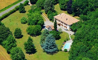 Vista aérea de uma casa rodeada por vegetação exuberante, com uma piscina e um gramado bem cuidado.