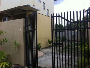 Uma entrada com portão para um edifício, com um caminho de concreto que leva a uma área de estacionamento.