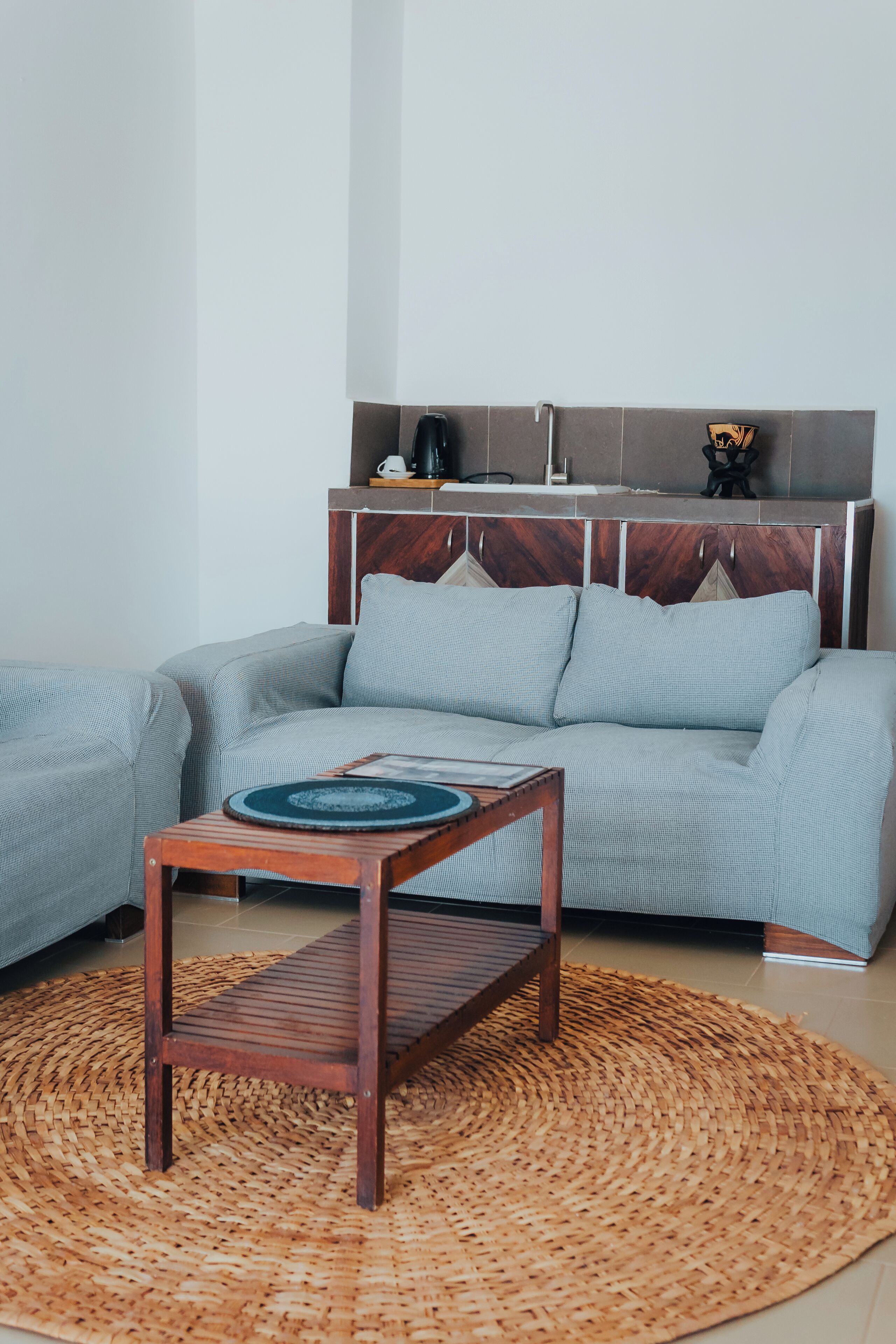 Uma sala de estar moderna com um sofá cinzento, uma mesa de centro de madeira e um tapete tecido.