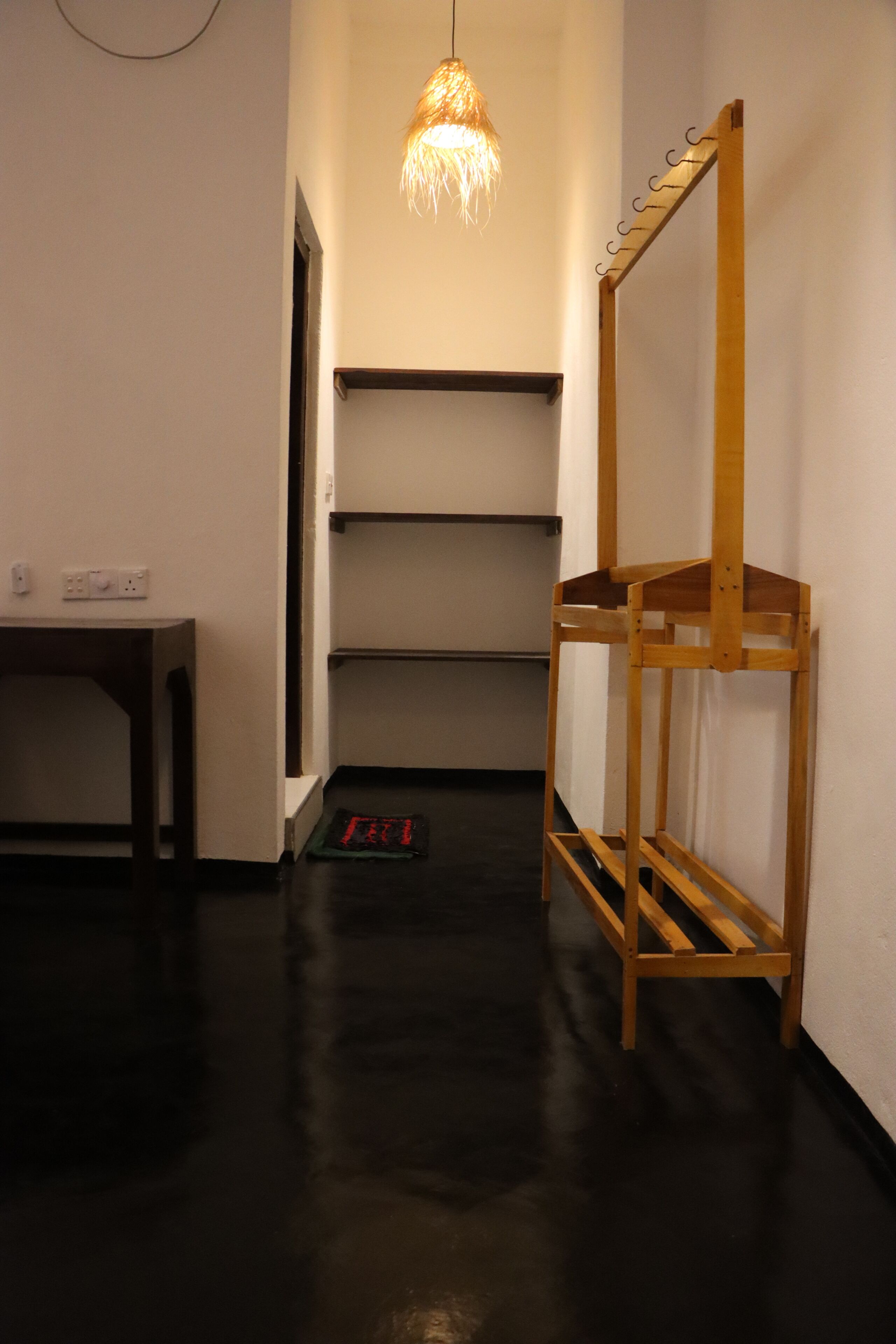 Um corredor com um suporte de madeira, uma luminária pendente e uma pequena mesa com um objeto vermelho.