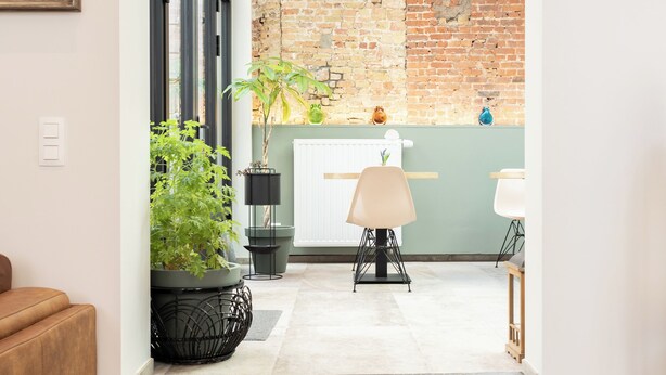 Interior moderno com parede de tijolos, balcão de recepção e área de estar com uma planta.