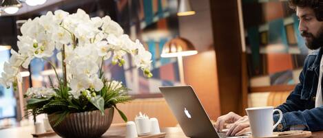 Uma pessoa trabalhando num laptop em cima de uma mesa de madeira, com uma orquídea em vaso e uma caneca branca.