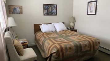 Quarto de hotel com cama, uma cadeira, mesa de cabeceira e duas luminárias fixadas na parede.