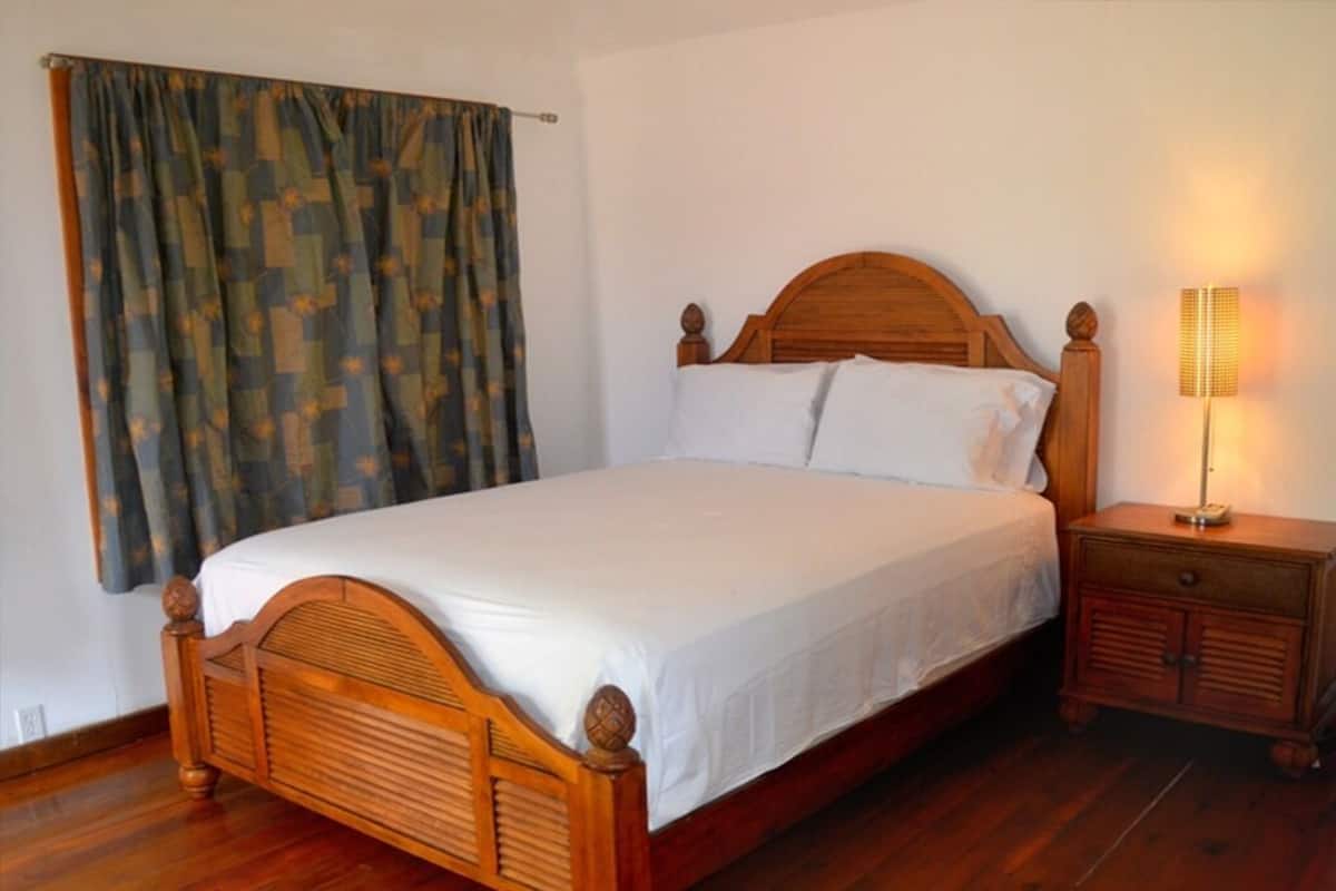 Uma cama bem arrumada com cabeceira de madeira, uma mesa de cabeceira com abajur e uma cortina com padrão geométrico.