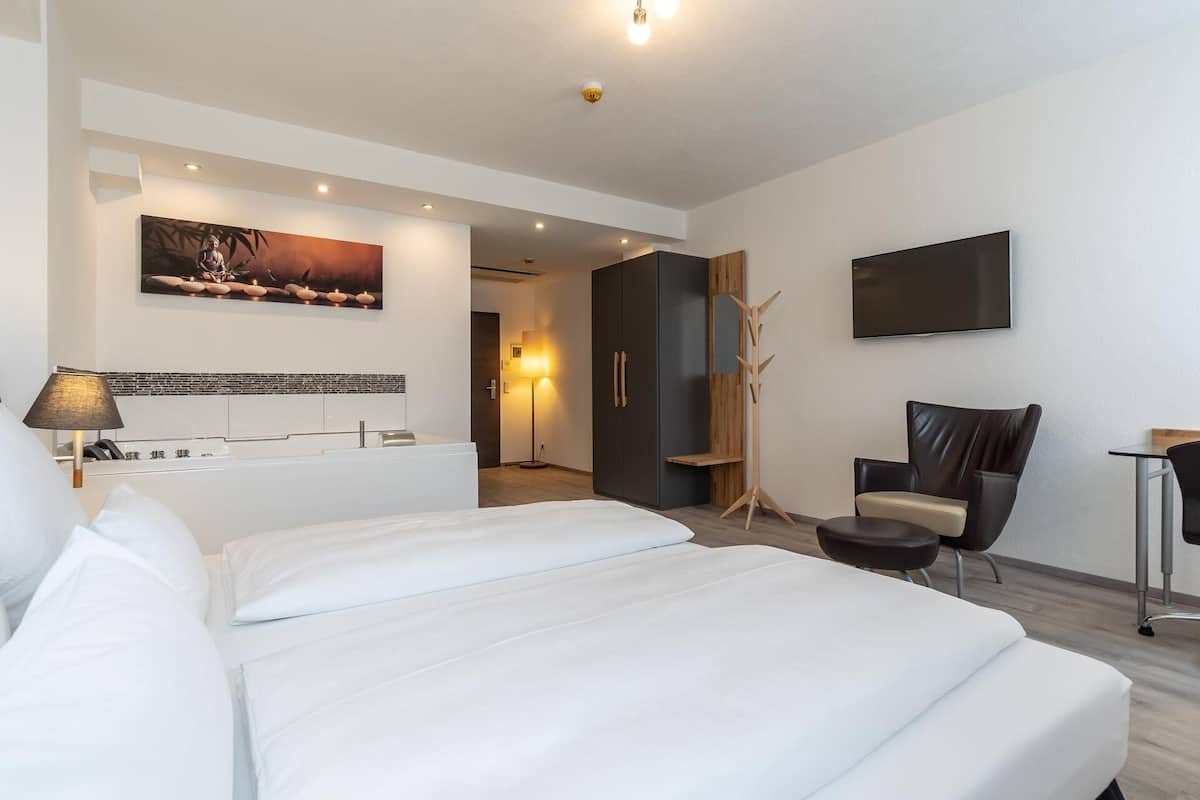 Um quarto moderno com uma cama grande, uma escrivaninha, uma cadeira e uma televisão.