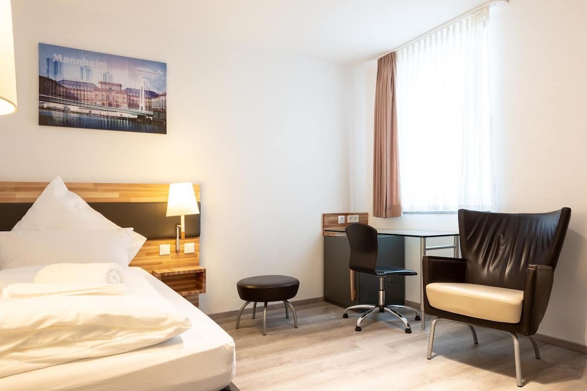 Quarto de hotel com cama, escrivaninha, cadeira e vista para a cidade.