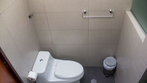 Um banheiro pequeno e moderno com vaso sanitário, lixeira e barra de apoio na parede.