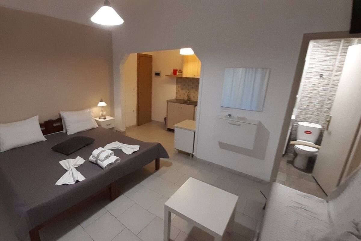 Quarto de hotel com cama, uma mesa pequena, cozinha compacta e banheiro.