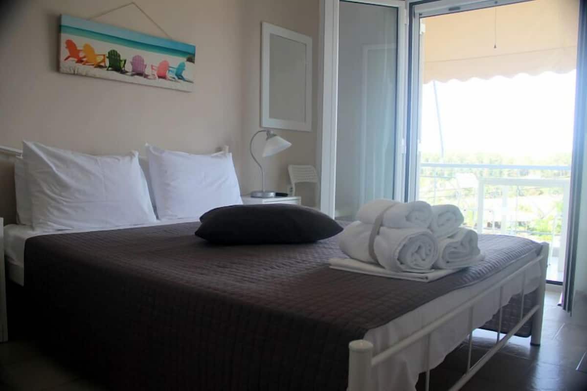 Quarto de hotel com cama, pintura, luminária e varanda com vista.
