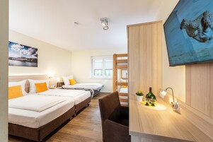 Quarto de hotel com uma cama, uma mesa com um computador, uma cadeira, uma janela e um quadro na parede.