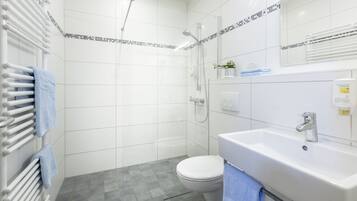 Uma casa de banho moderna com uma sanita, chuveiro e lavatório branco.