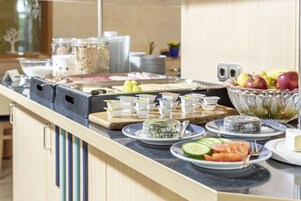 Uma mesa de buffet com diversas opções de comida, incluindo frutas, legumes e uma variedade de pratos em bandejas.